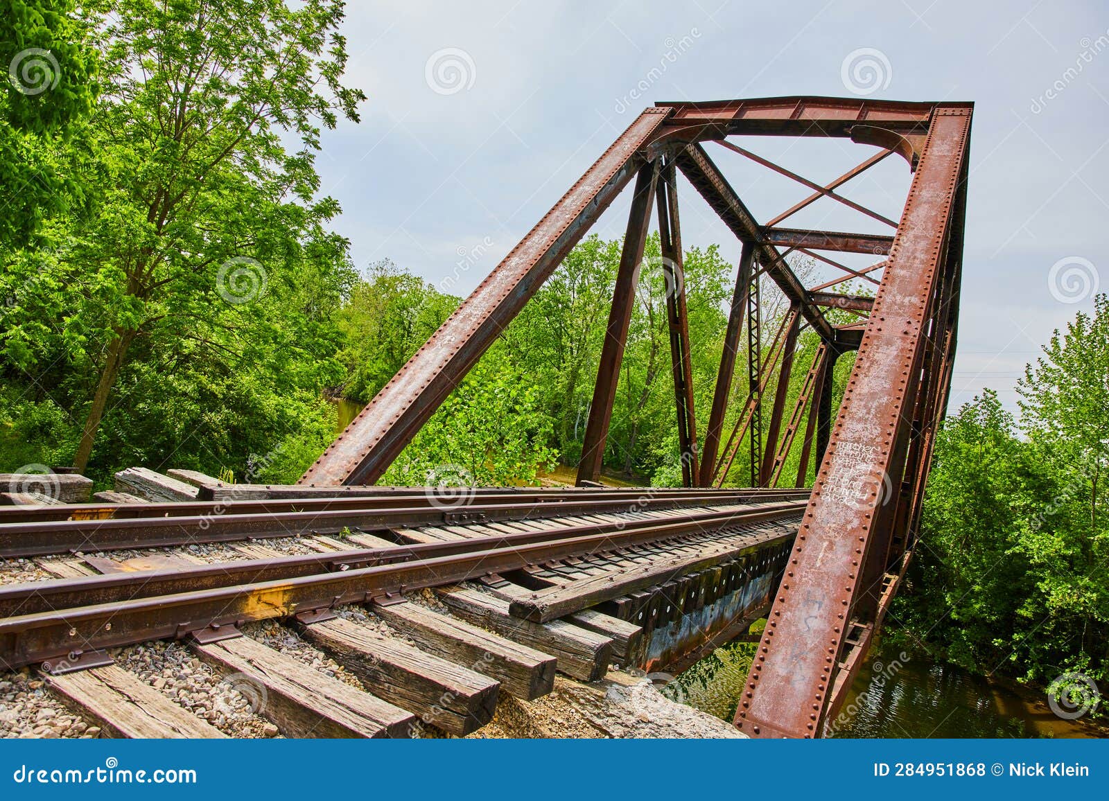 Tilted View of Rusty Iron Railroad Bridge Over River Leading into Lush ...