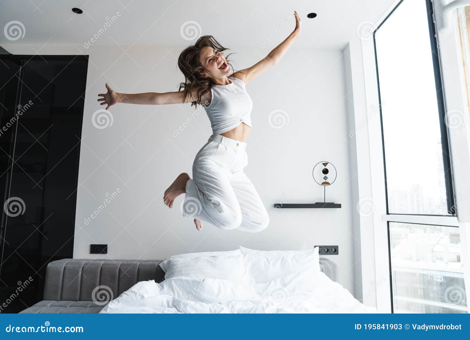 Image of Young Excited Woman Making Fun and Jumping on Bed Stock Image ...