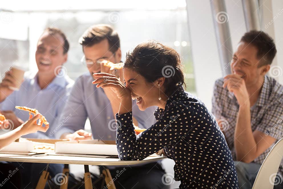 Indian Woman Laughing Eating Pizza With Diverse Coworkers In Off Stock