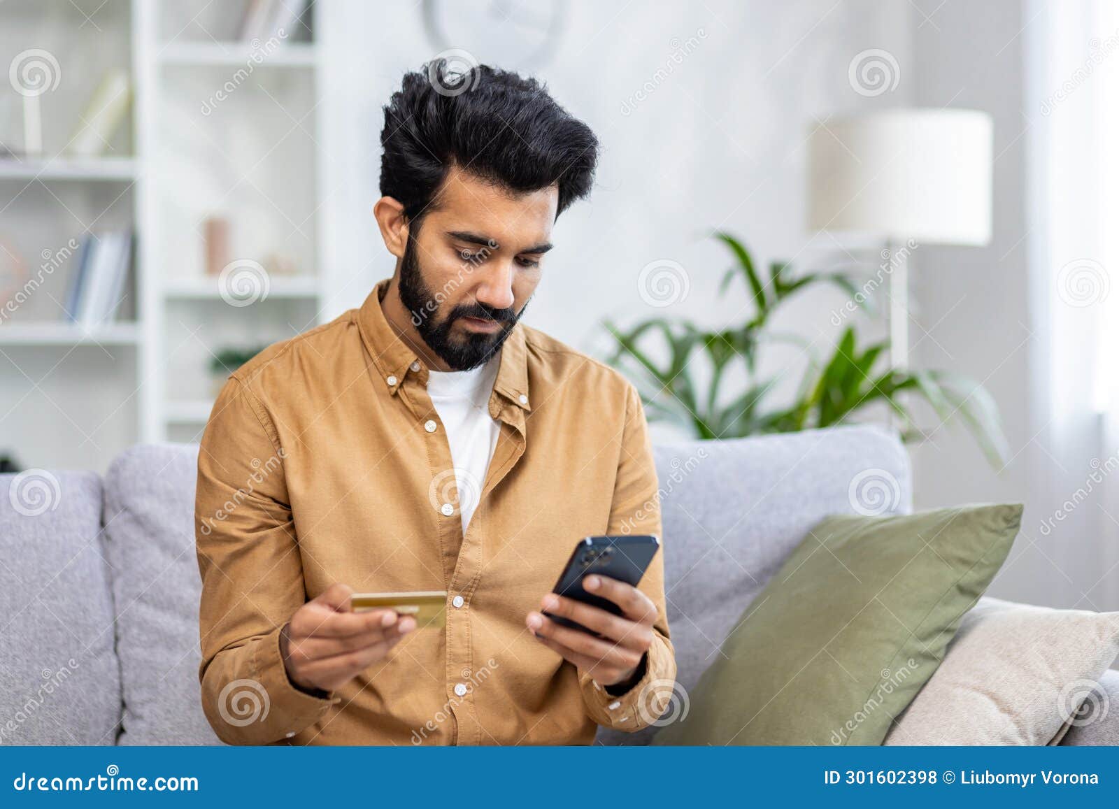 Indian Young Man Sitting on Sofa at Home and Using Mobile Phone and Credit Card Stock Photo ...