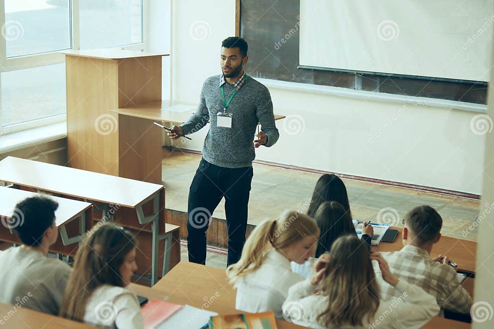 Interactive Learning Session. Young Teacher Leading Lecture in Front of Classroom, Engaging with ...