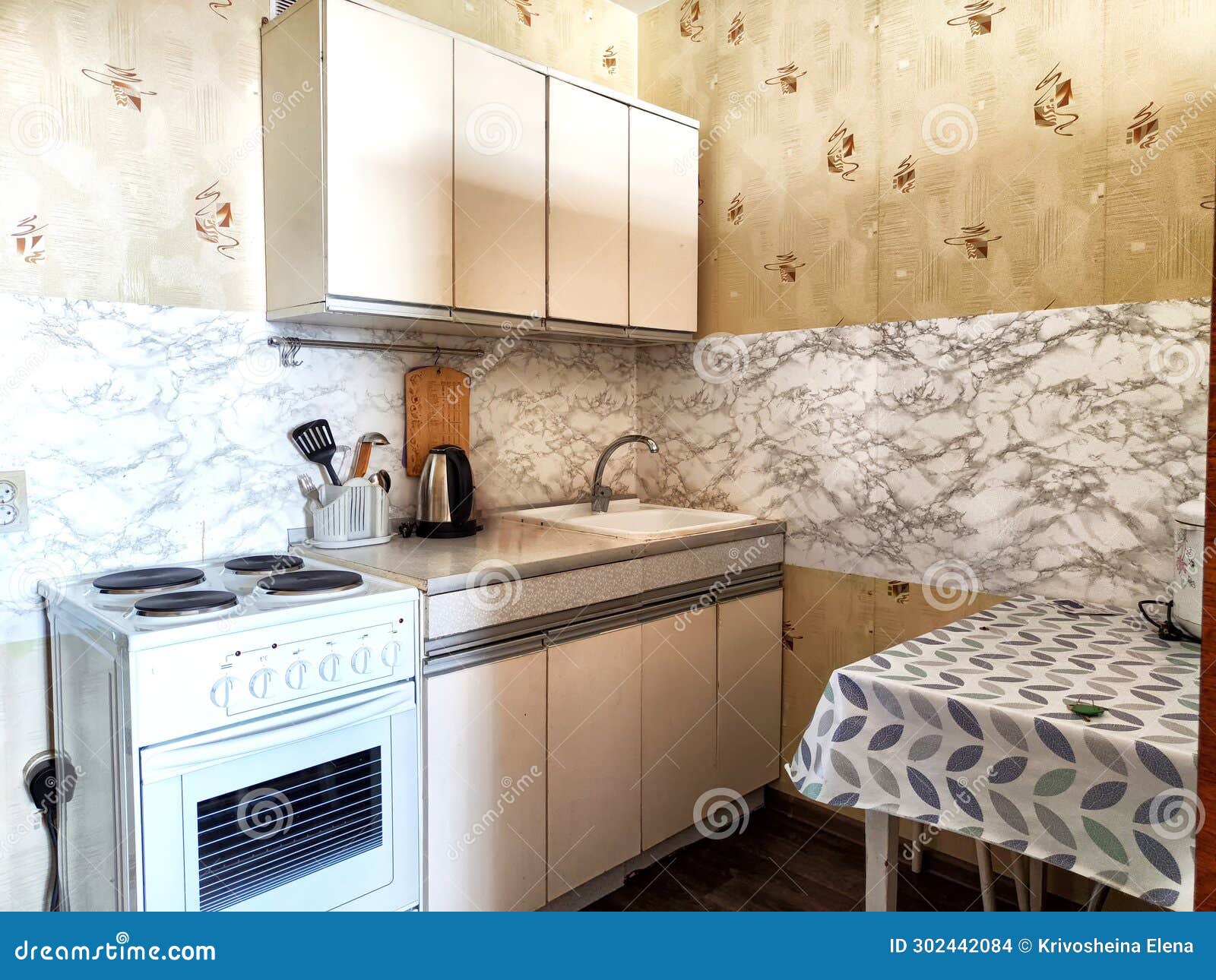 The Interior is a Small Old Kitchen with a Table, Stool, Cabinets, Sink ...