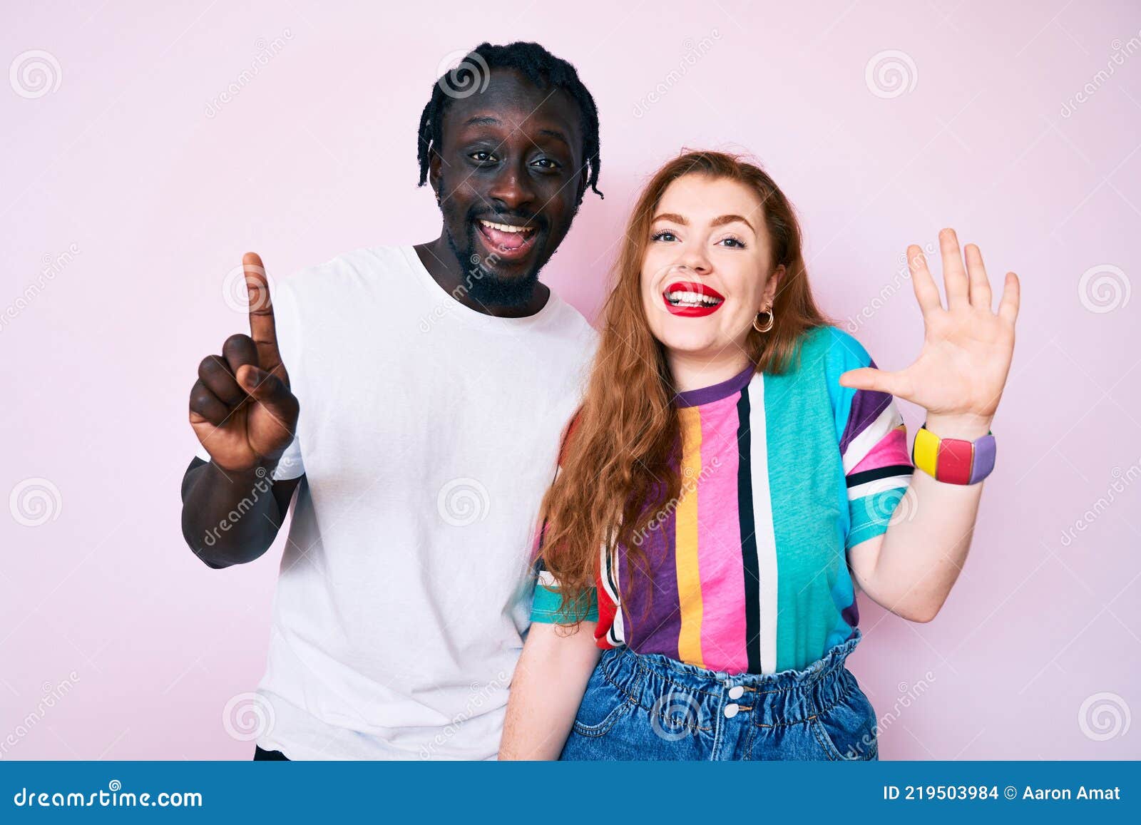 Interracial Couple Wearing Casual Clothes Showing And Pointing Up With