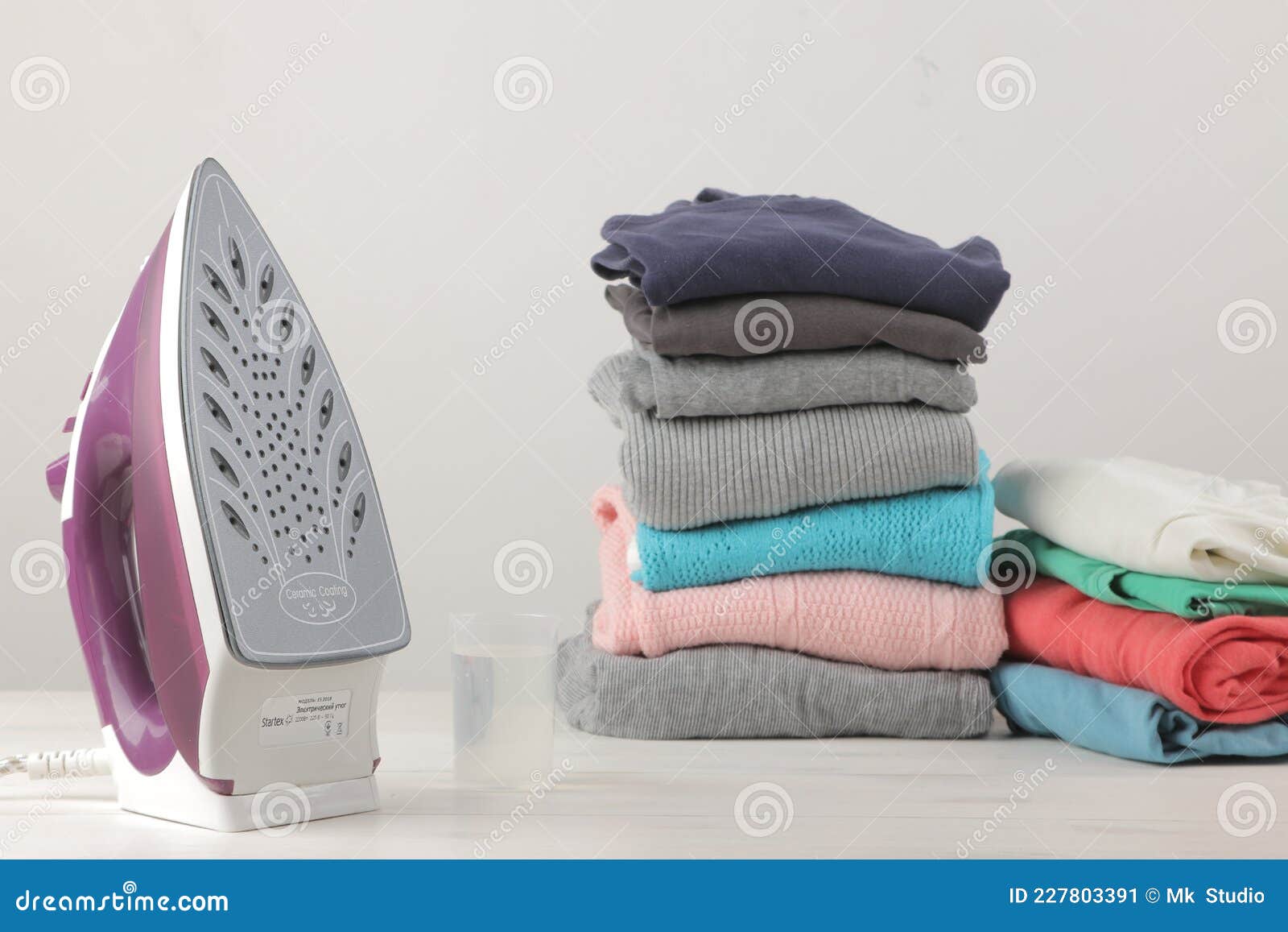 Iron and a Stack of Colored Clothes on a White Background. Ironing of ...