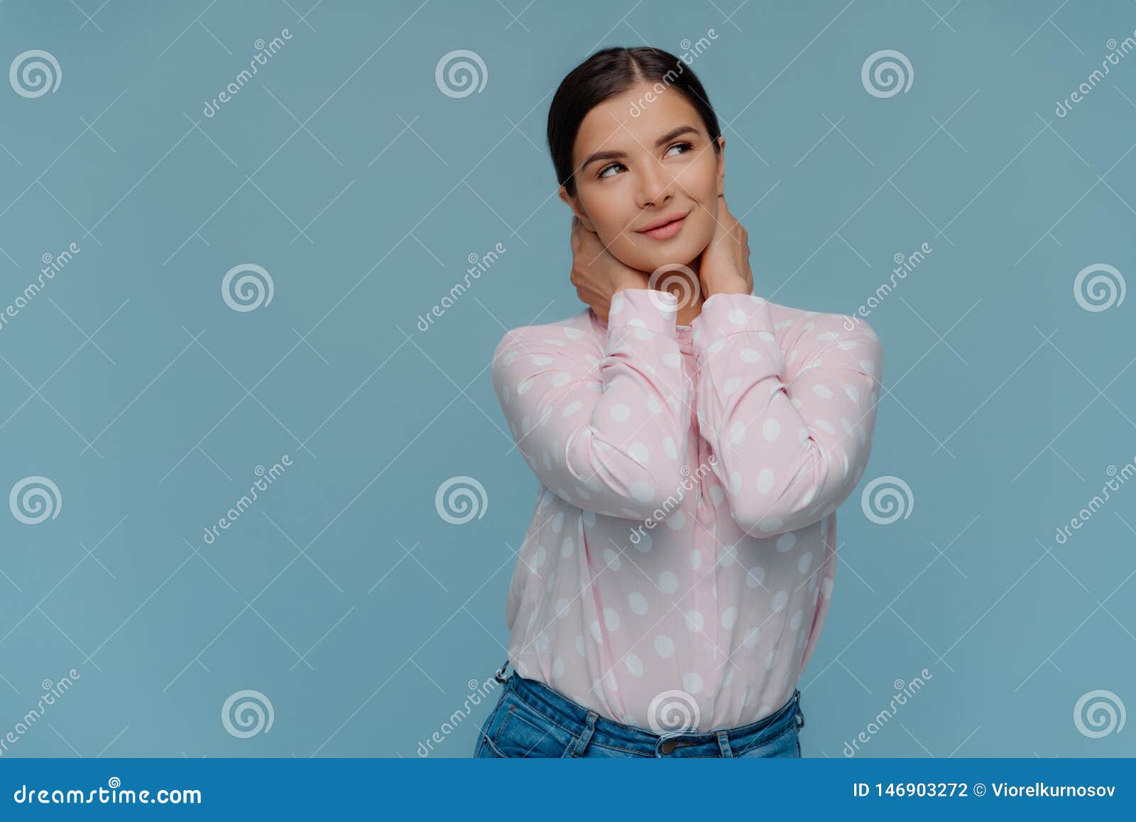 Isolated Shot Of Cute Dark Haired Woman Keeps Hands On Neck Behind