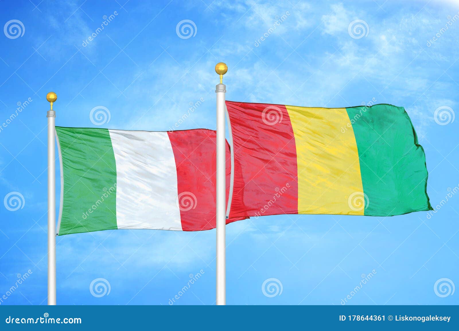 Italy and Guinea Two Flags on Flagpoles and Blue Cloudy Sky Stock Image ...