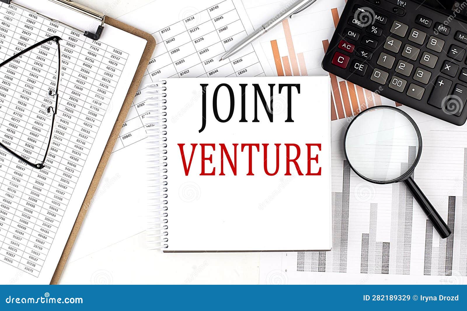 JOINT VENTURE Text on Notebook with Clipboard and Calculator on a Chart ...