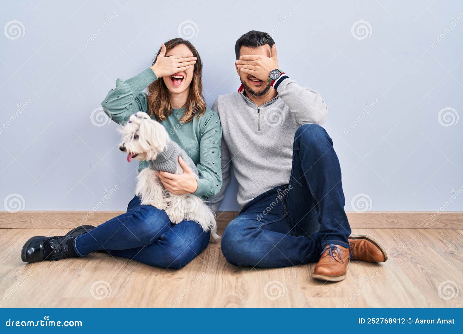 Joven Pareja Hispana Sentada En El Suelo Con Un Perro Sonriendo Y Riendo Con La Mano En La Cara