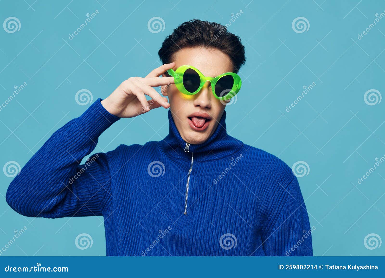 A Joyful Man Stands On A Light Blue Background In A Blue Zip Up Jacket