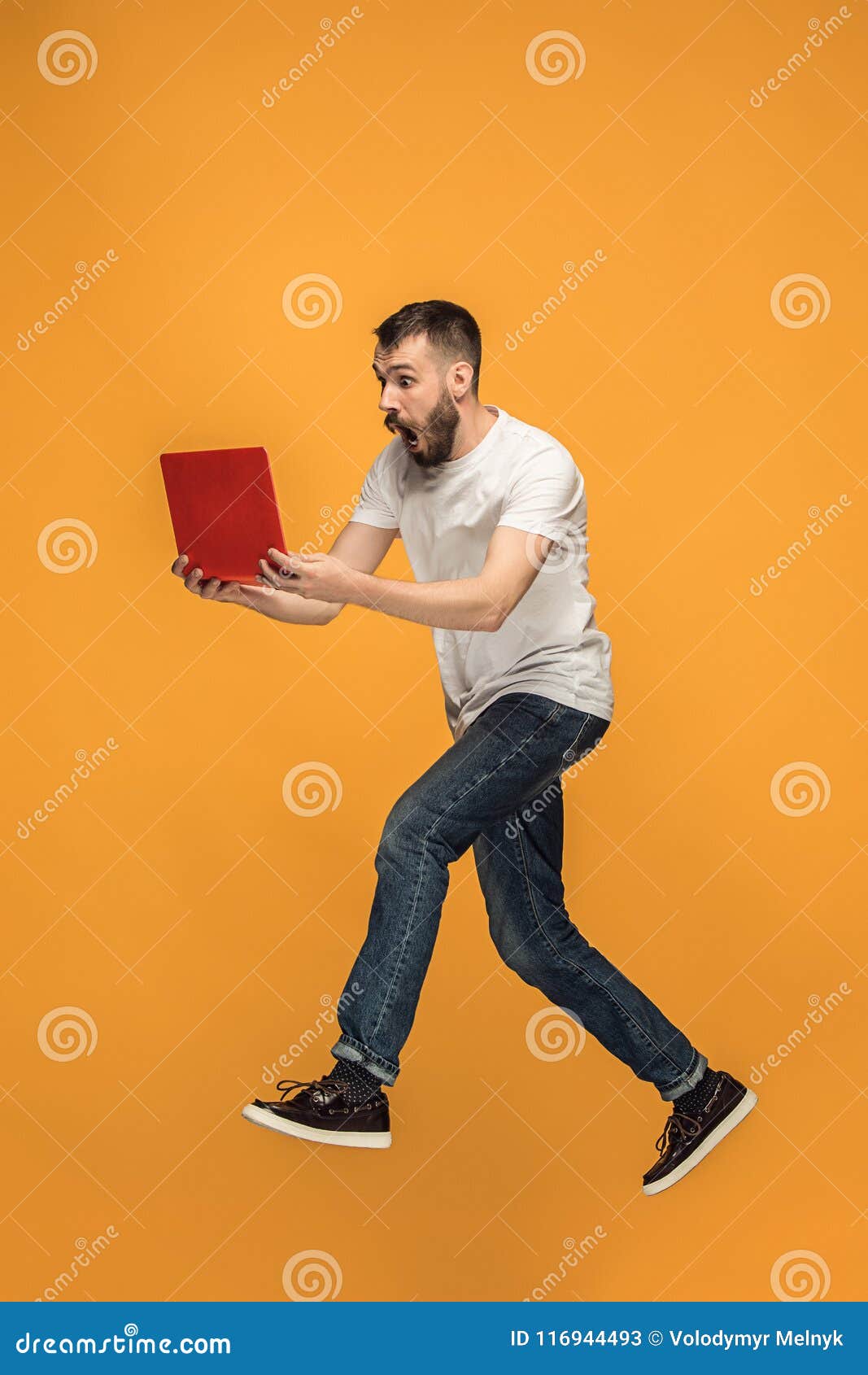 Image of Young Man Over Orange Background Using Laptop Computer while ...