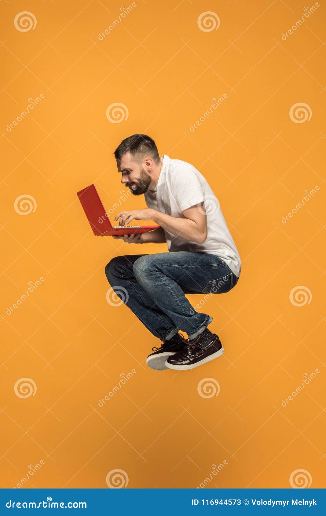 Image of Young Man Over Orange Background Using Laptop Computer while ...