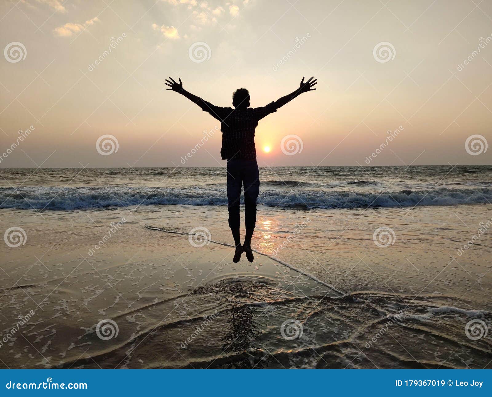 Jumping with Hands Wide Open Facing the Setting Sun at a Beach Stock ...