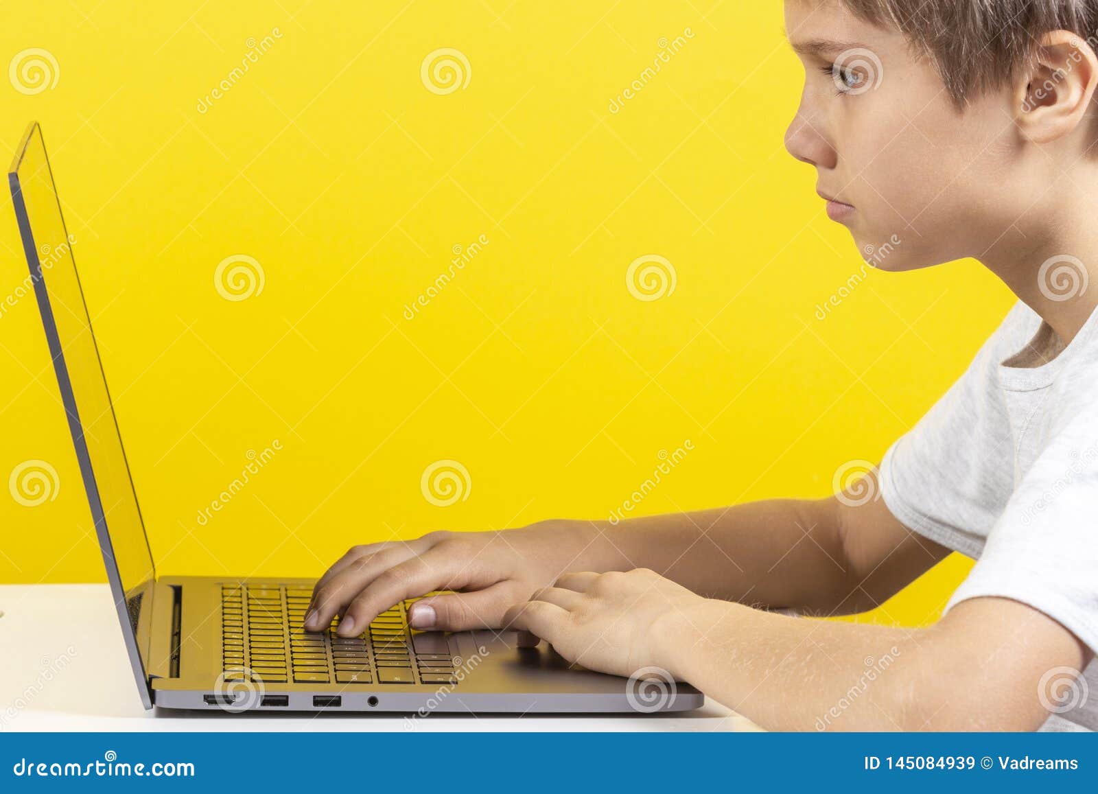 Kid Sitting at the Table and Using Laptop Computer, Yellow Background ...