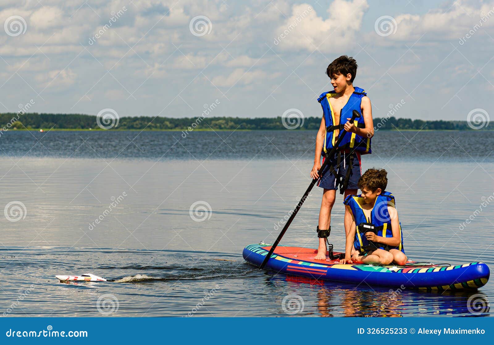 Kids on a SUP Paddleboard on the Lake are Playing with an RC Model Boat ...