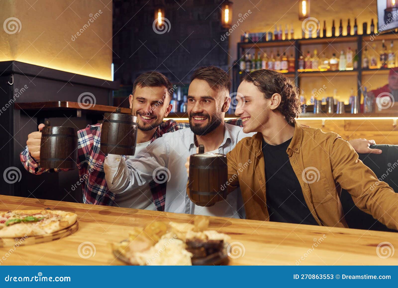 Knocking the Mugs. Three Friends are in the Bar Drinking Beer and ...