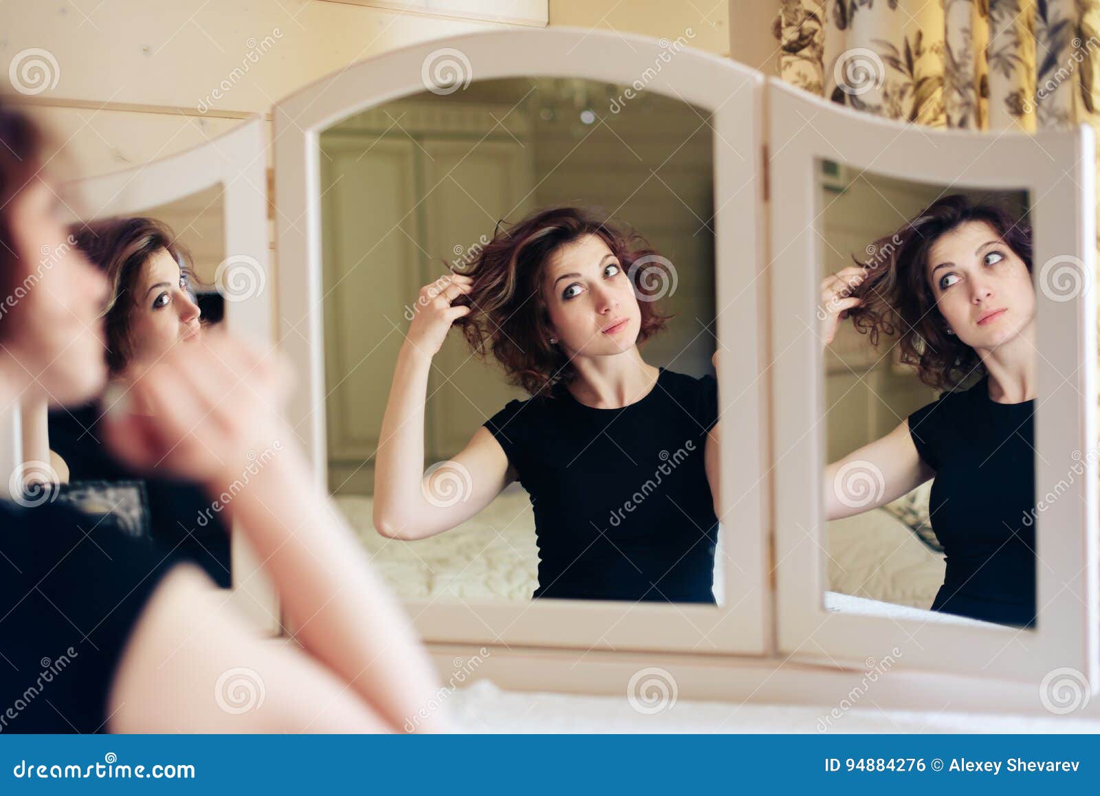 La Chica Joven Hermosa En Un Vestido Negro Se Sienta Delante De Un Espejo Del Vintage Reflejado