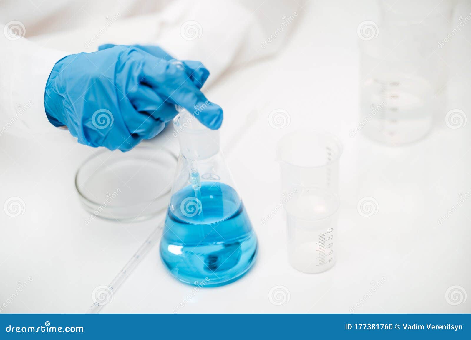 Lab Assistant in Rubber Gloves Pointing To Flask with Blue Liquid on ...