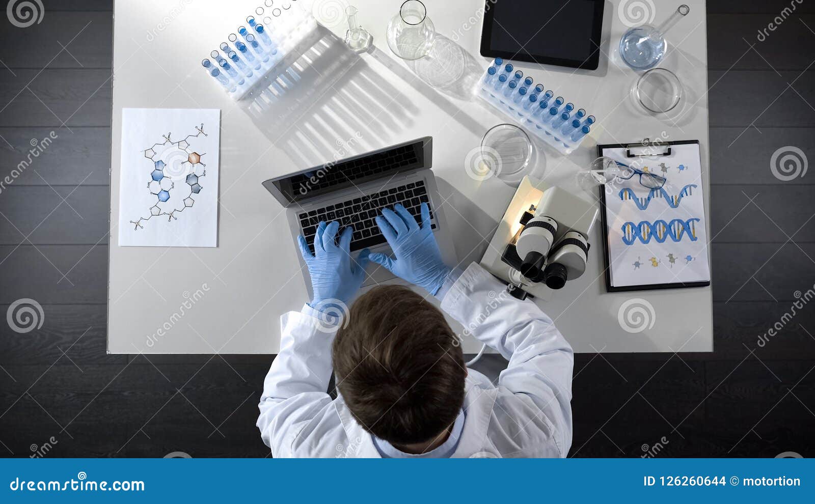 Lab Worker Viewing Samples Under Microscope and Typing Results on ...