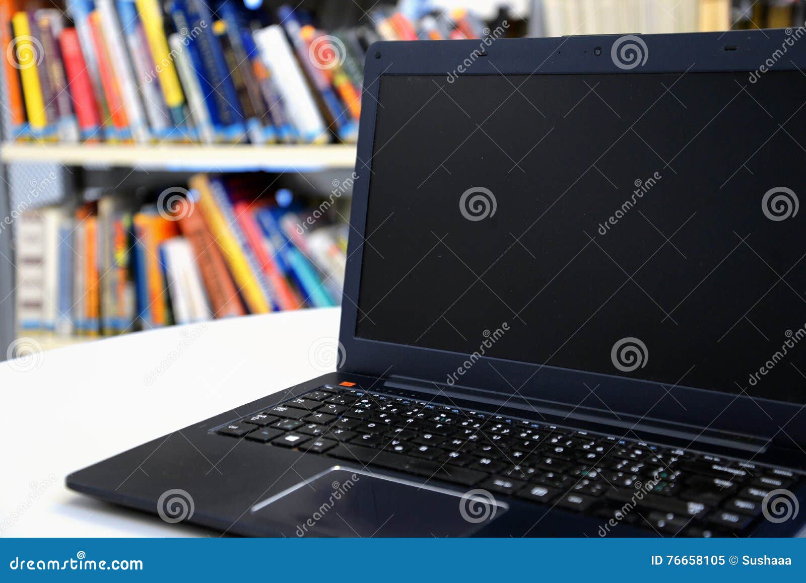 Laptop in the Library. Compture on the Table. Bookshelves in the ...