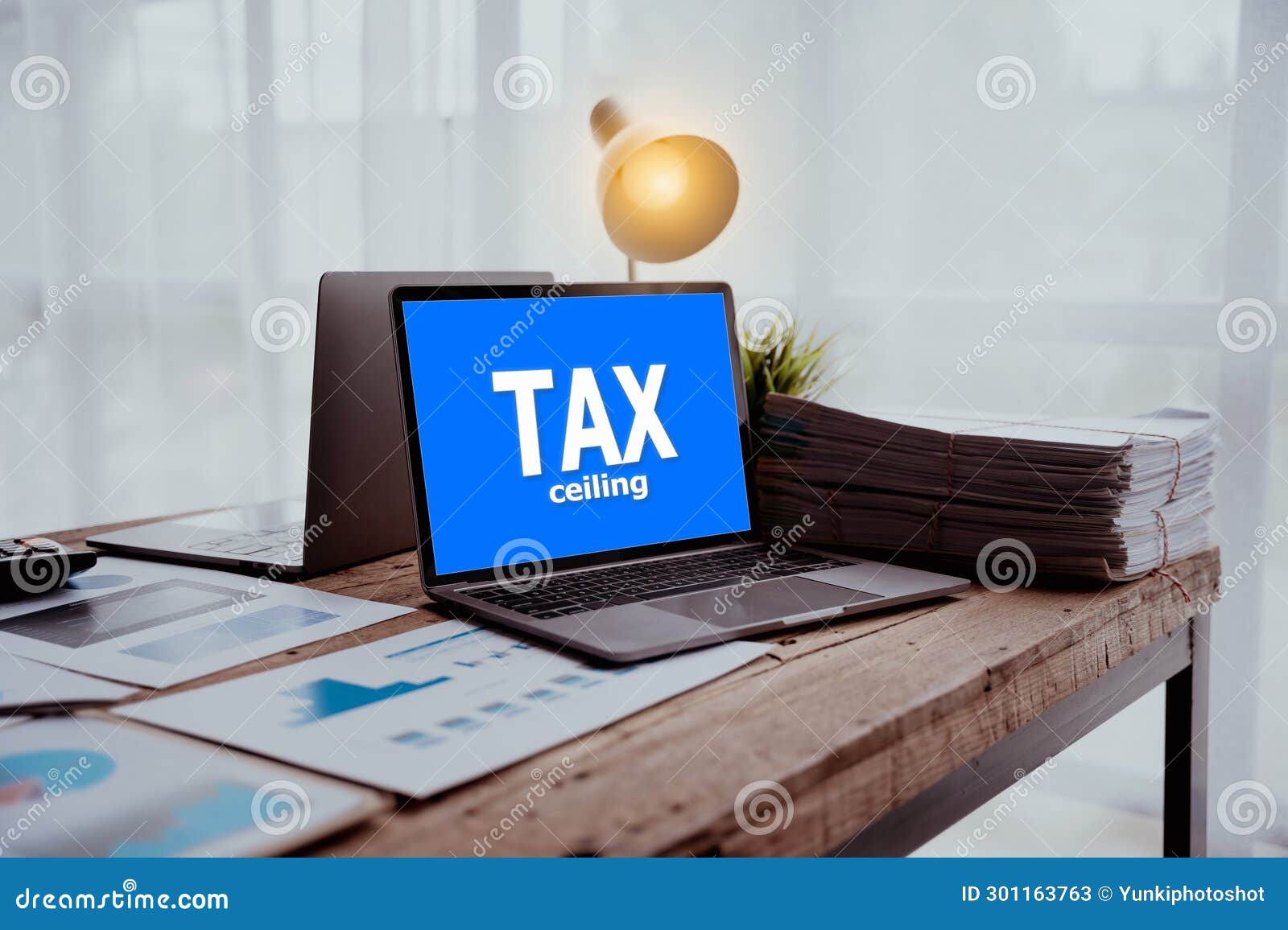 Laptop with the Word "TAX Ceiling" on the Screen, a Lamp, and a Stack ...