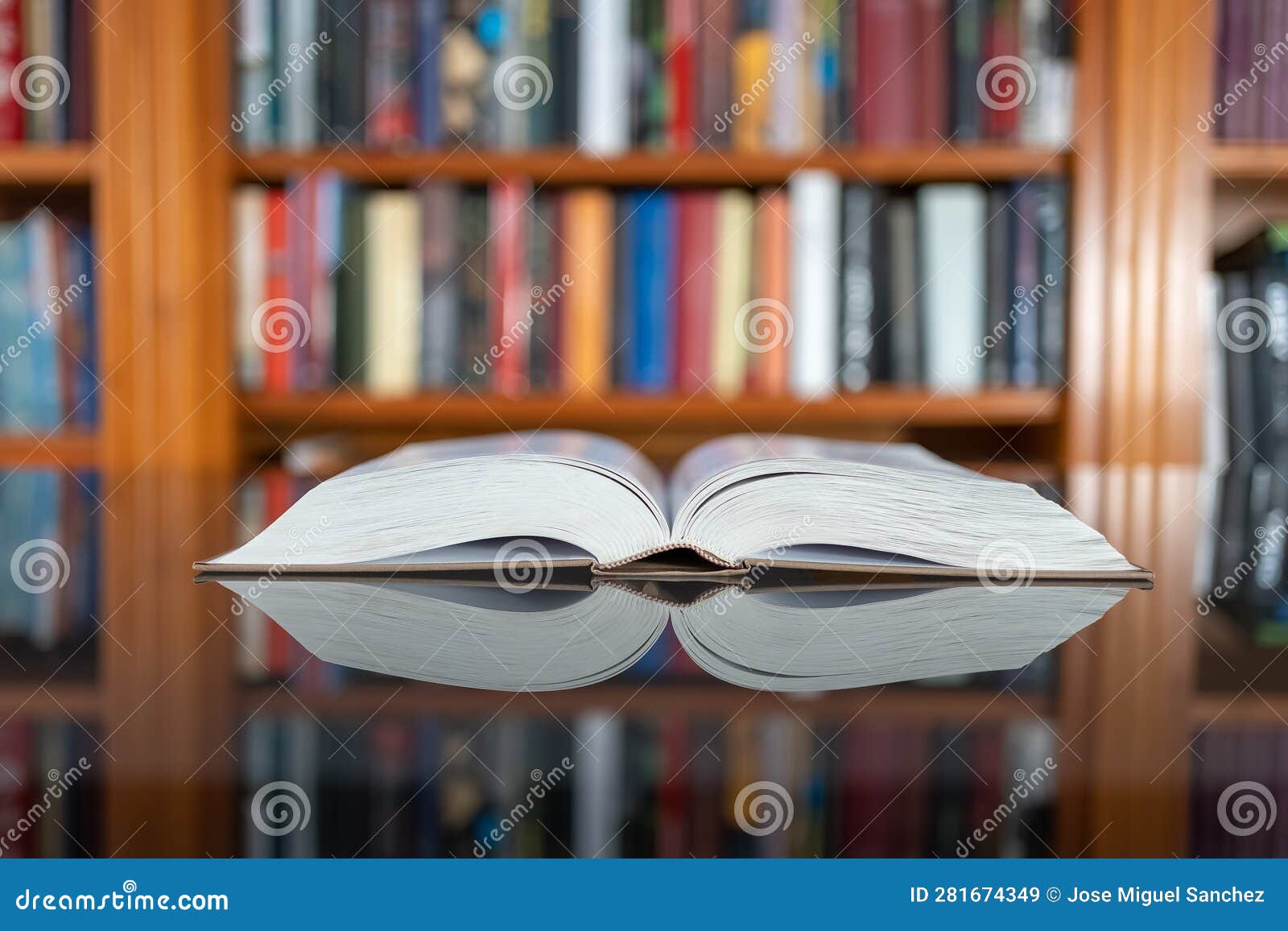 Large Open Book on Top of a Glass Table with a Library Full of Books in ...