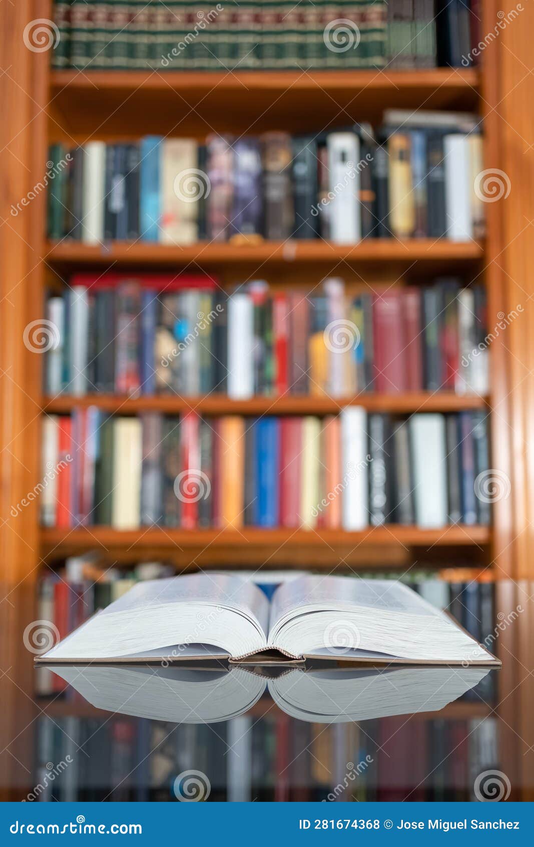Large Open Book on Top of a Glass Table with a Library Full of Books in ...