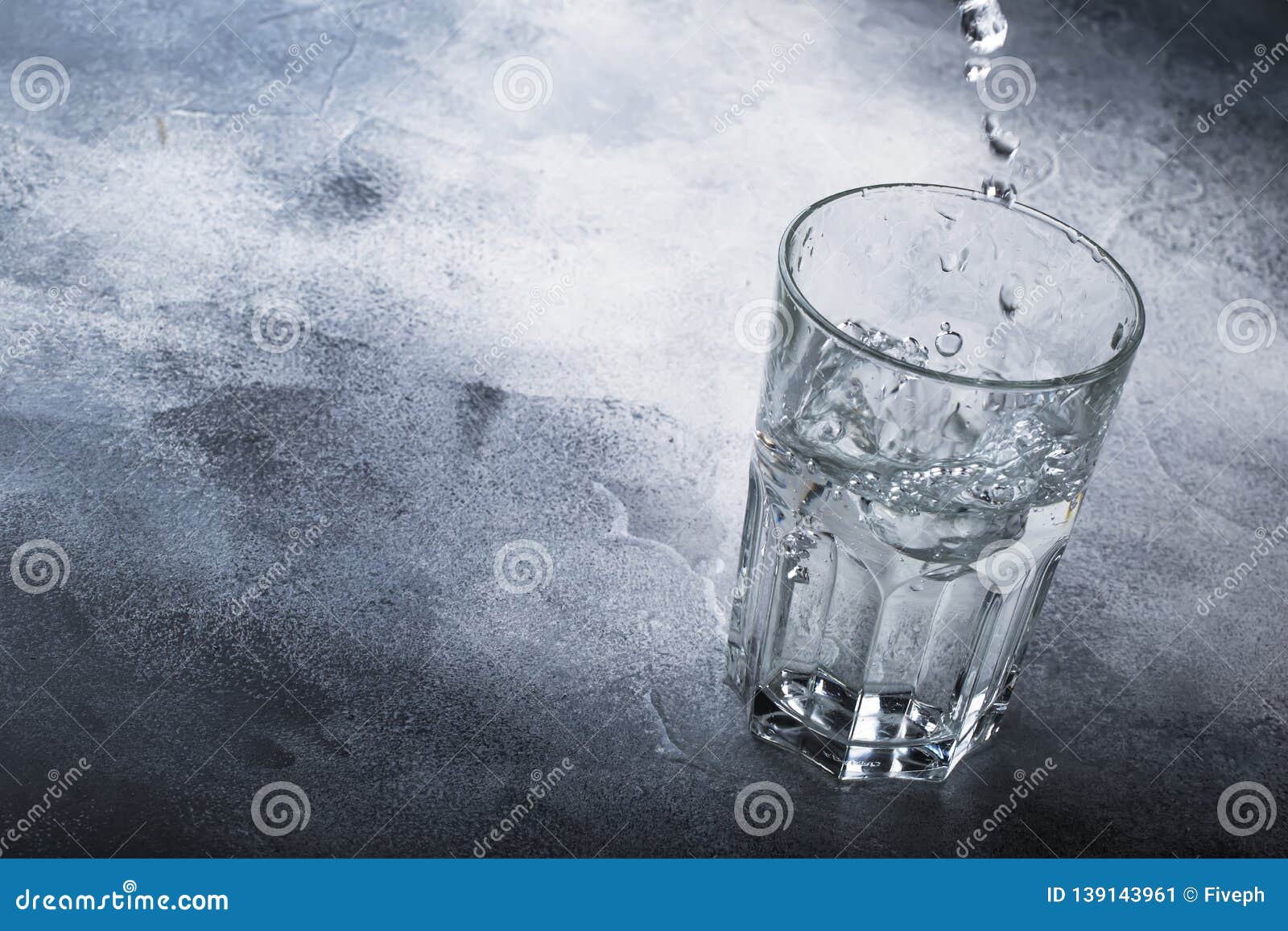 Last Drops of Pure Water are Poured into Large Glass Cup on Gray Table ...