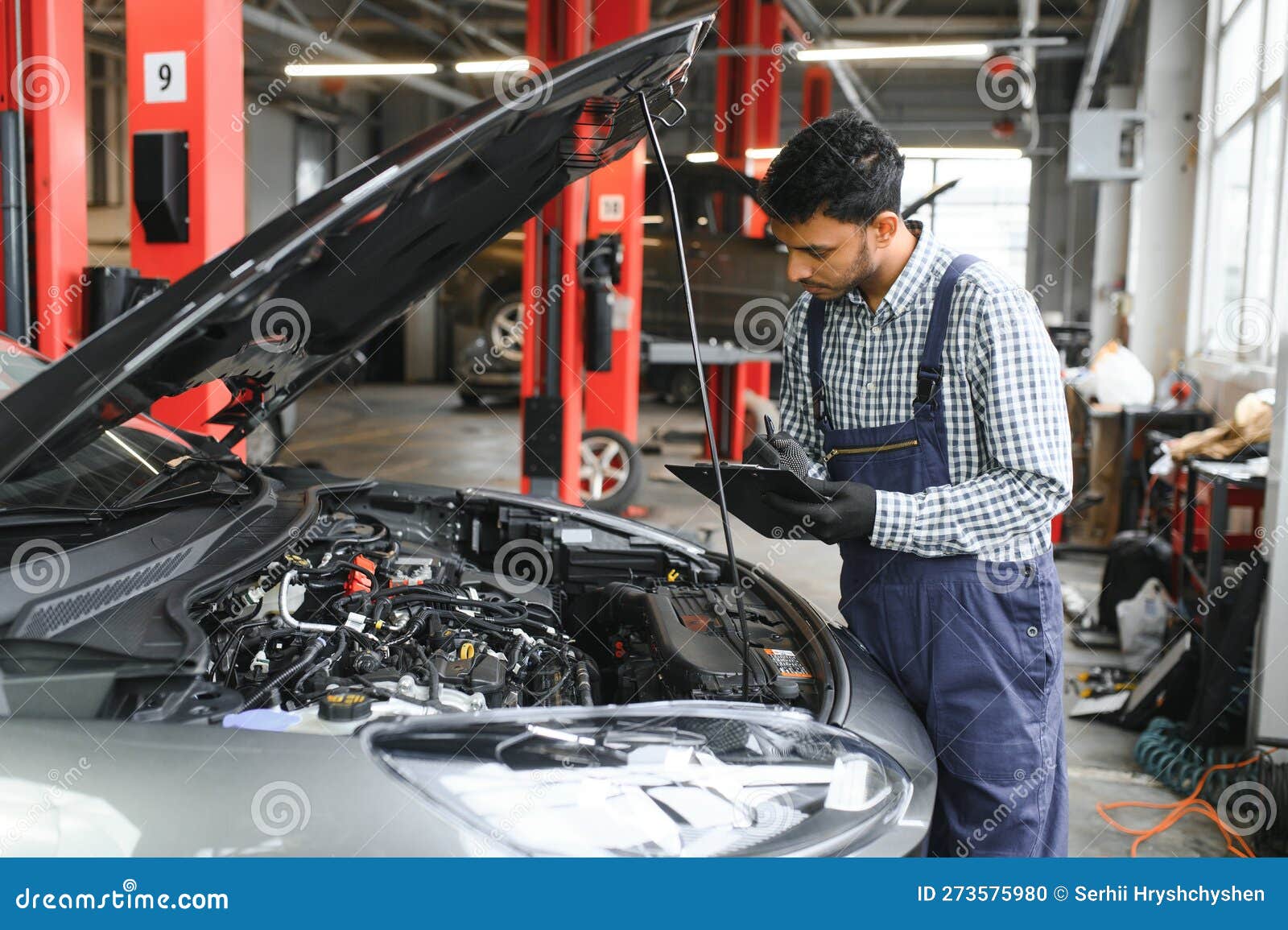 Latin Hispanic Auto Mechanic in Uniform is Examining a Car while ...