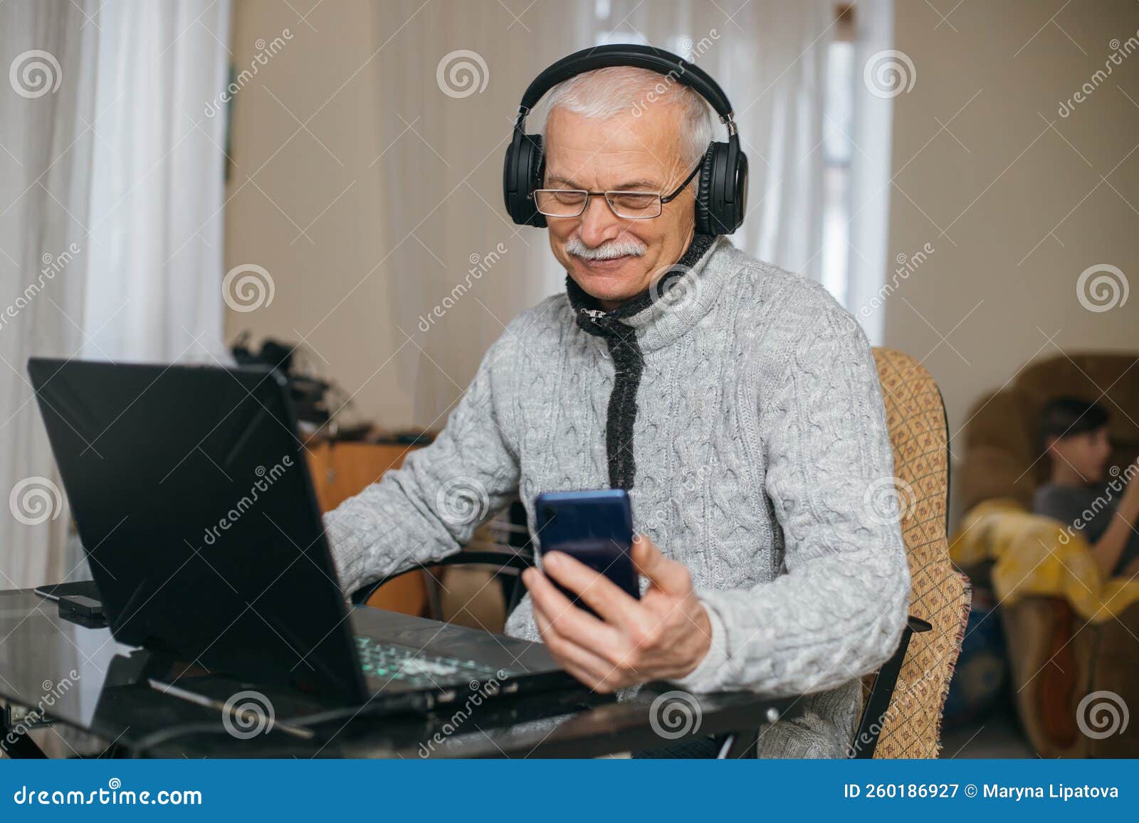 Elderly Man with Headphones Works Behind Modern Laptop. Old Man Holds ...