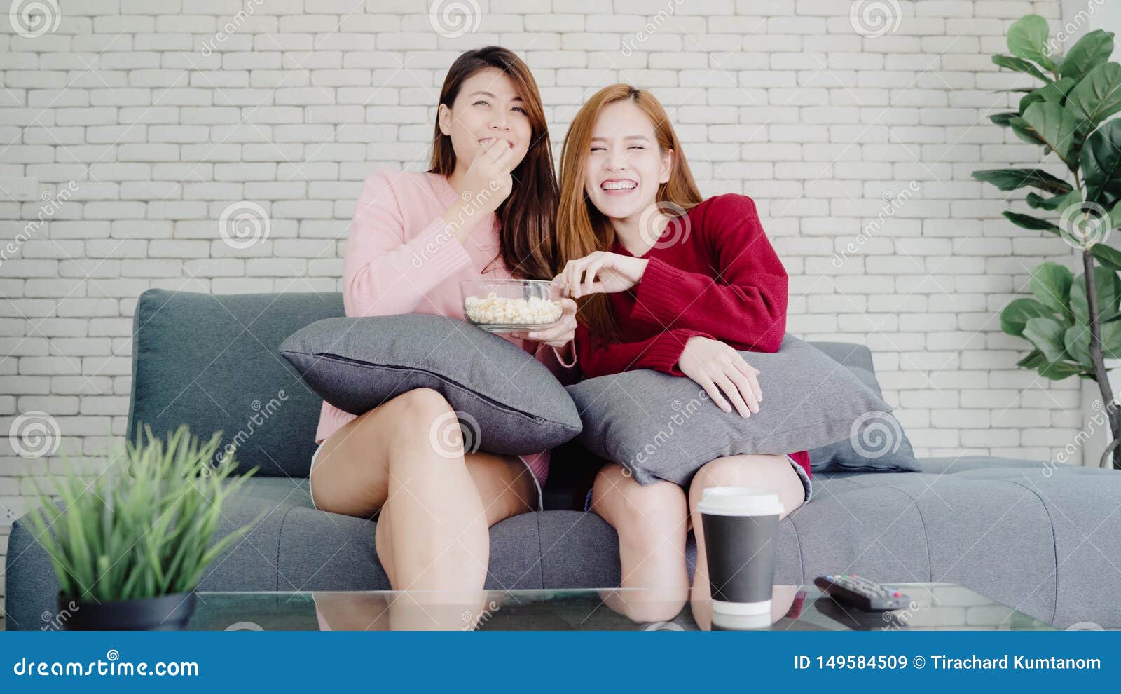 Lesbian Asian Couple Watching Tv Laugh And Eating Popcorn In Living