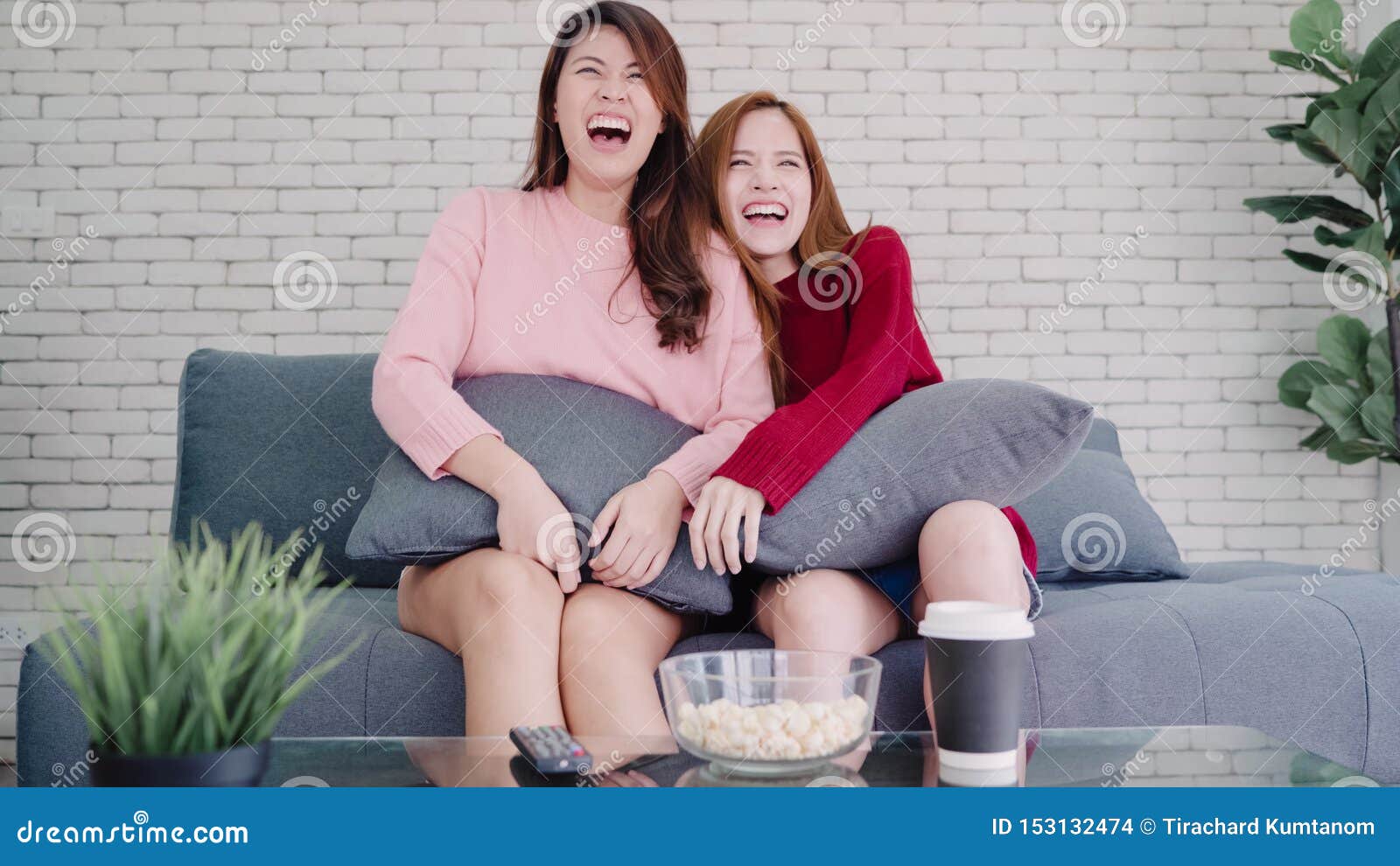 Lesbian Asian Couple Watching Tv Laugh And Eating Popcorn In Living