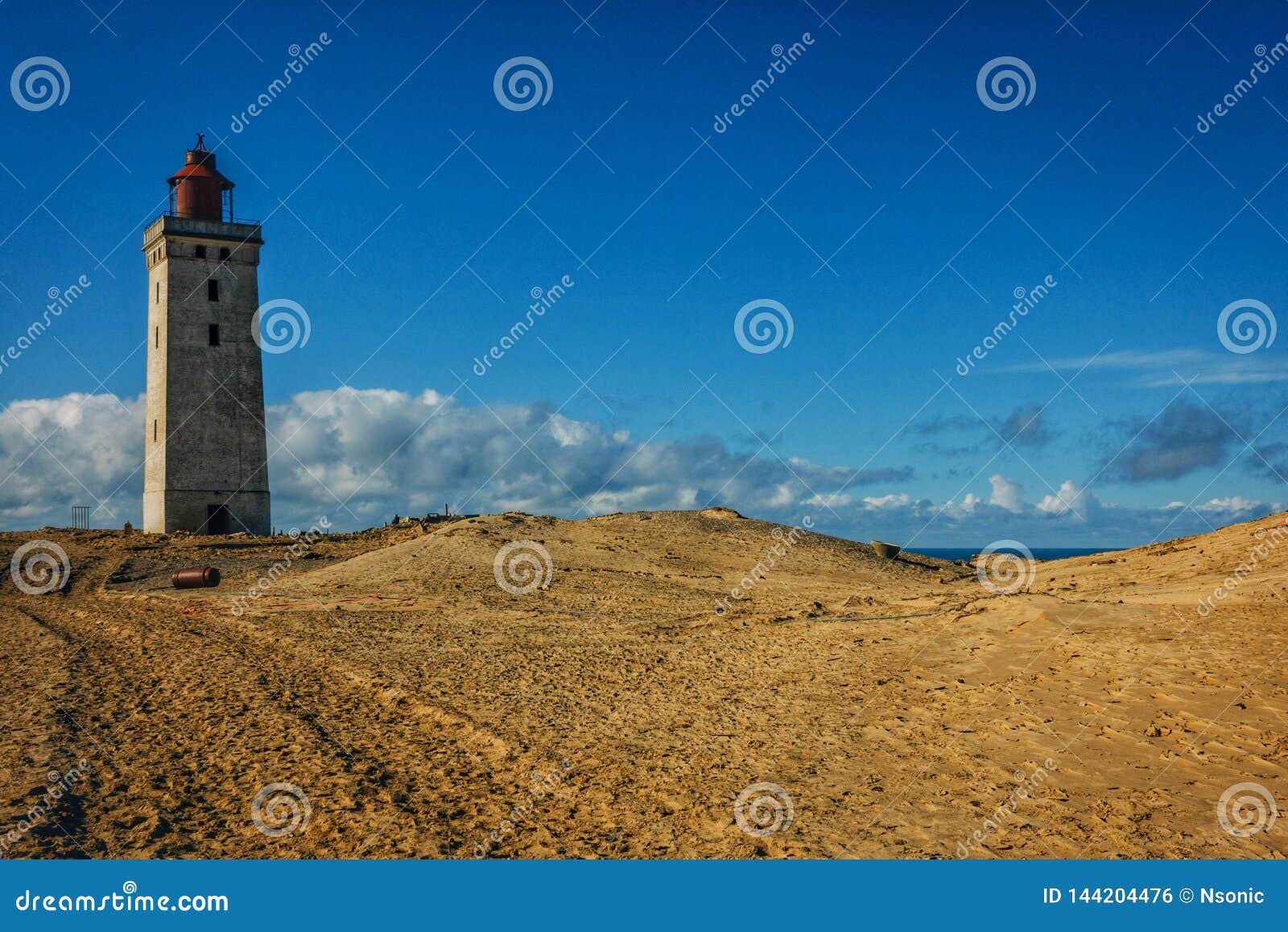 Lighthouse on sand dune stock photo. Image of clouds - 144204476