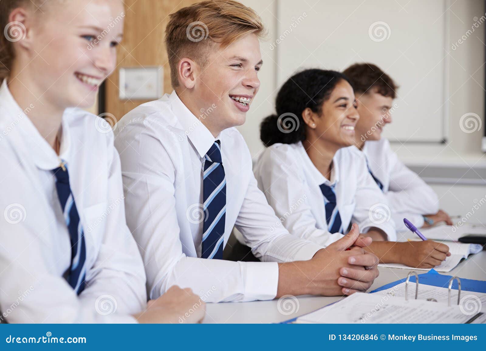 Line Of High School Students Wearing Uniform Sitting At Desk In ...