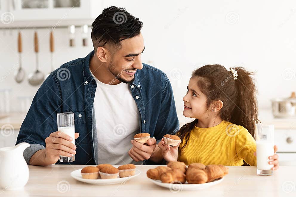 Little Arab Girl and Dad Holding Glasses with Milk and Eating Muffins ... Little Arab Girl and Dad Holding Glasses with Milk and Eating Muffins ...