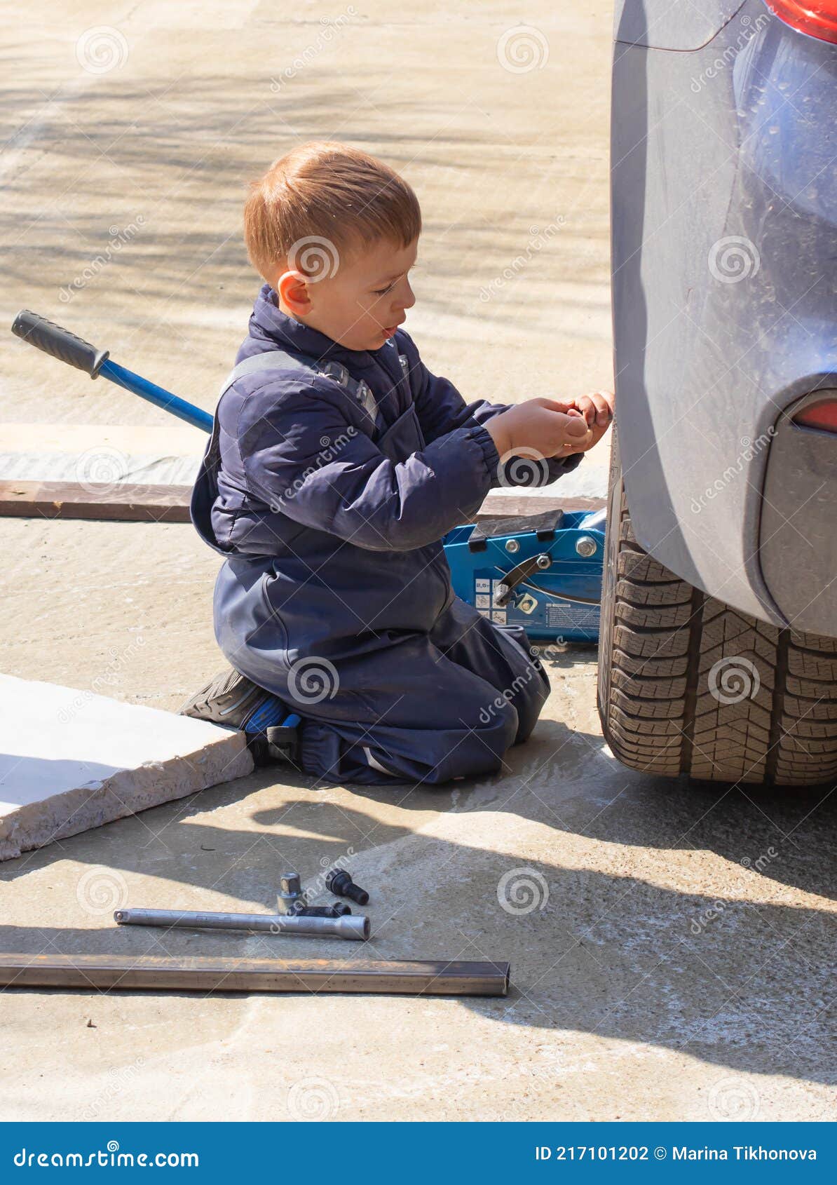 A Little Boy Fixes a Car, Changes a Wheel, Helps His Dad. Stock Photo ...