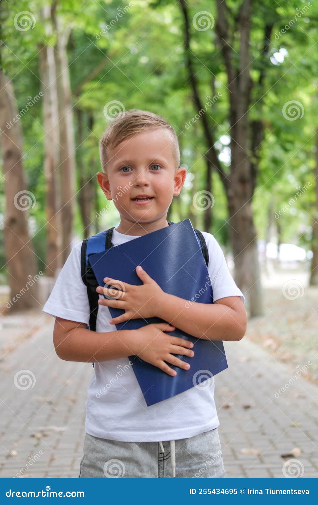 A Little Boy Holds a Notebook in His Hands with a Backpack on His Back ...