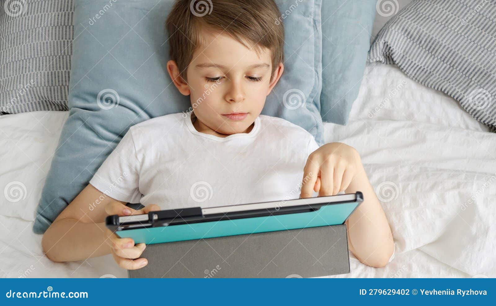 A Little Boy is Lying on His Bed and Playing with a Tablet Computer ...