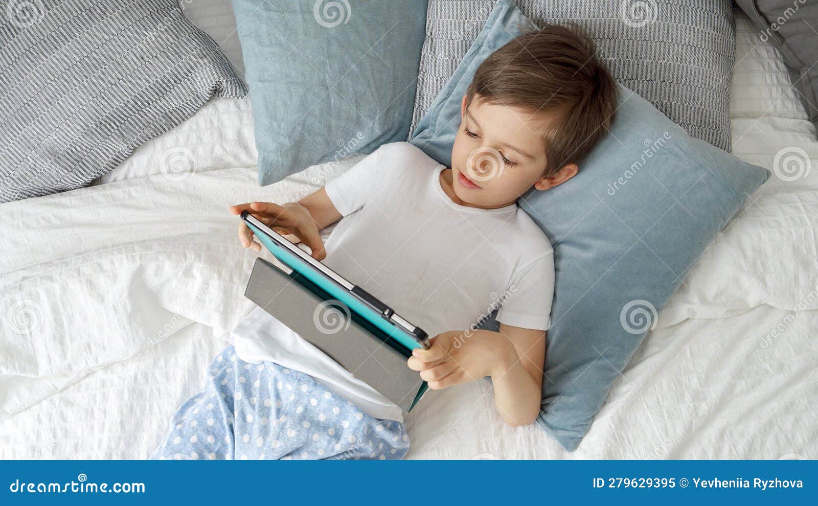 Little Boy is Lying on His Bed, Using a Tablet Computer during the Day ...