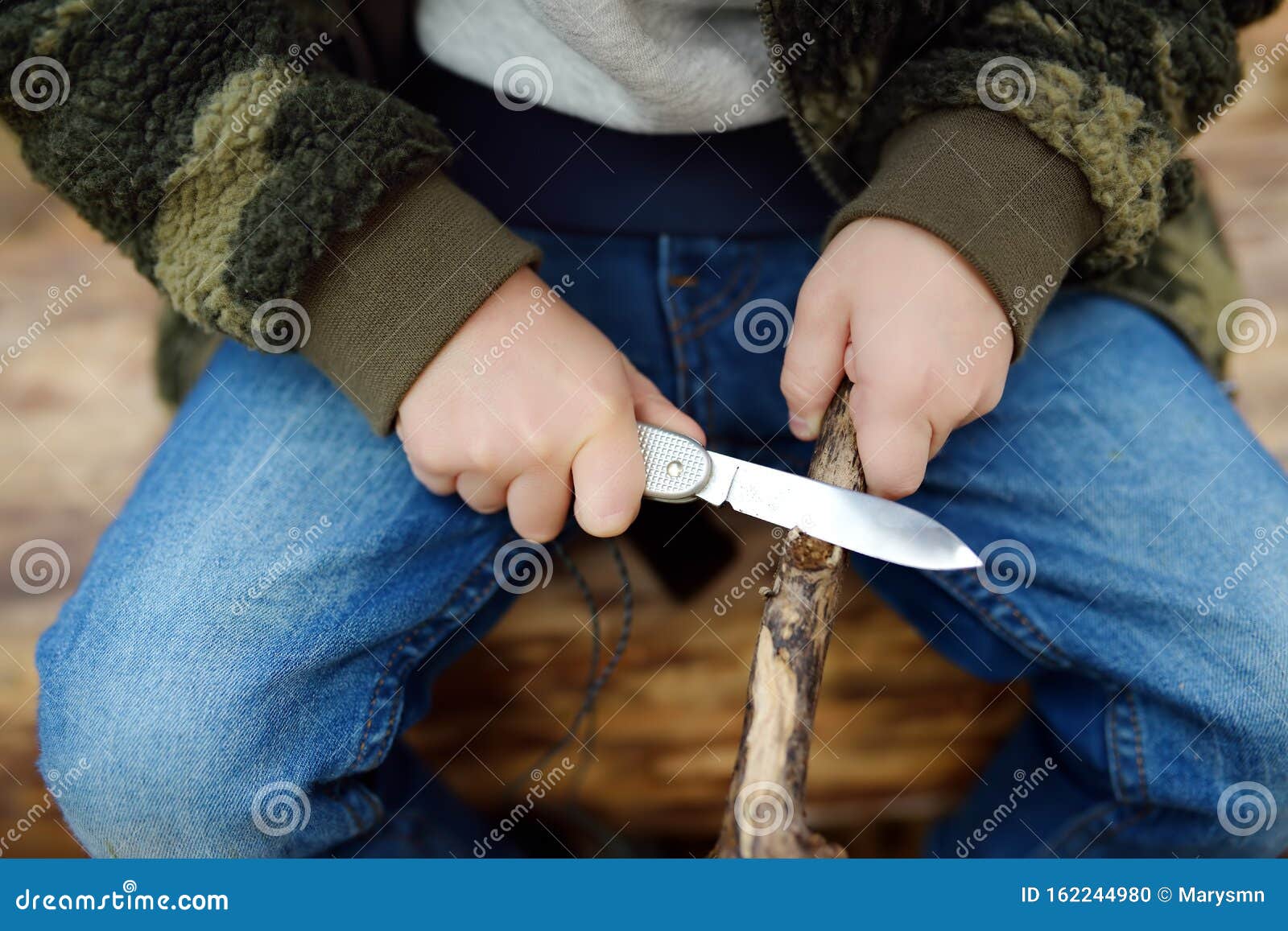 Little Boy Scout is Sharpening a Stick with the Help Knife in the ...