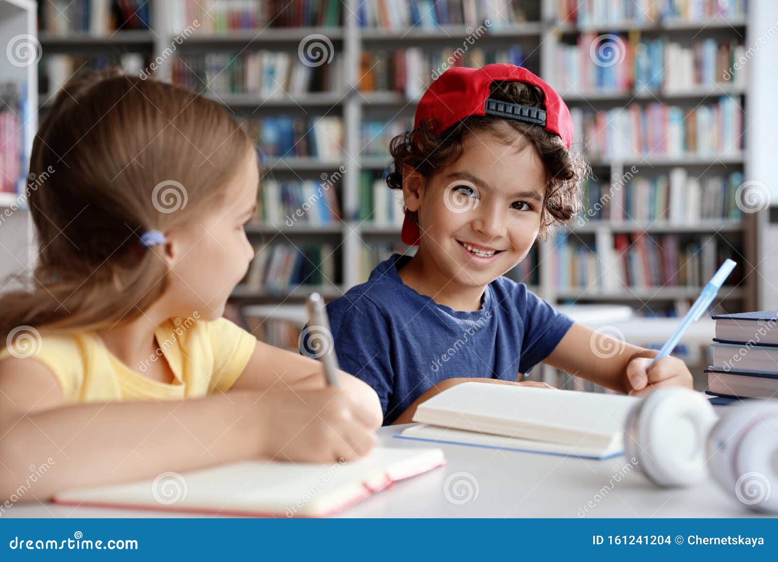 Little Children Writing at Table with Books in Library Stock Photo ...