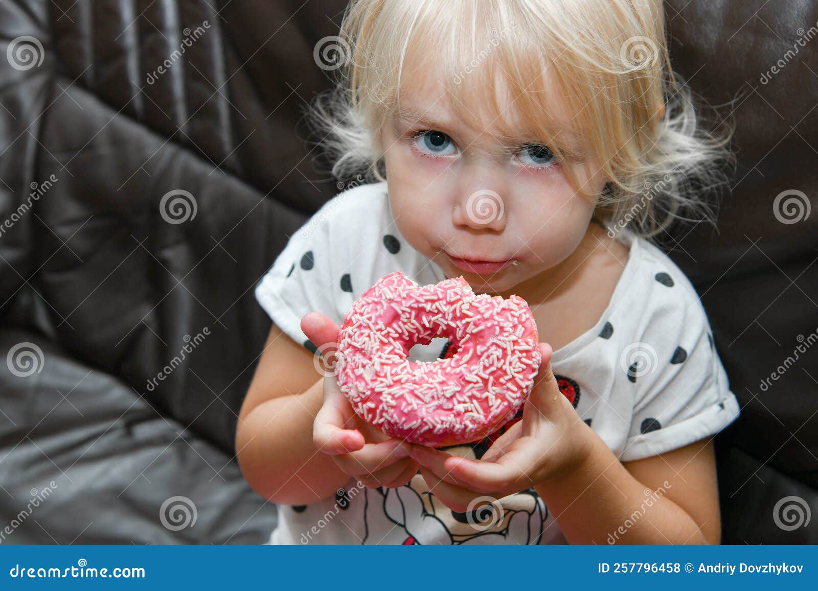A Little Girl Eats a Delicious Red Donut with Icing Stock Photo - Image ...