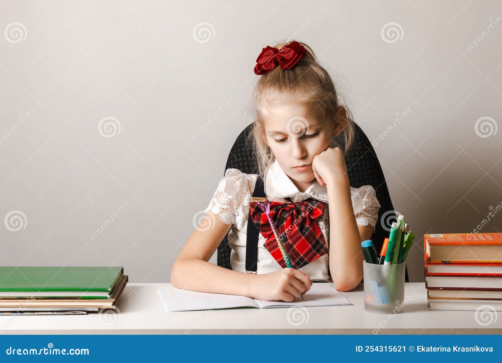 A Little Girl in a School Uniform is Doing Homework in a Exercise Book ...