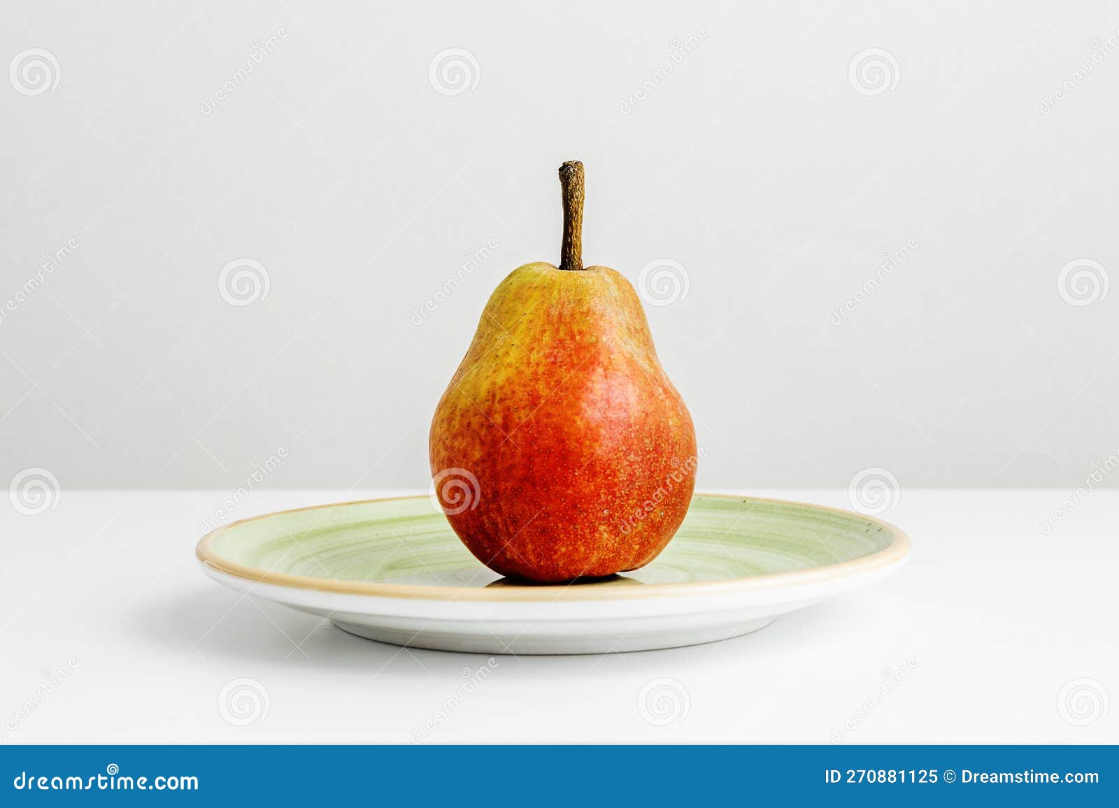 A Lone Ripe Pear on a Green Plate on a Plain White Surface and a White ...