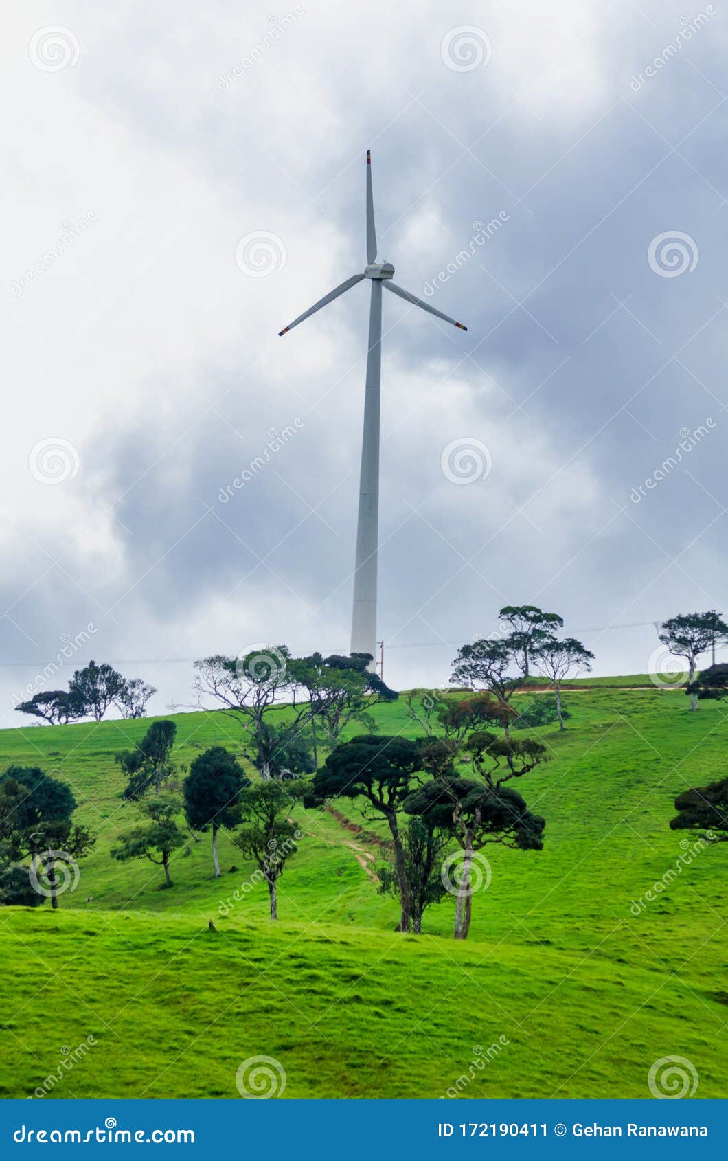 A Lone Windmill Standing Atop a Distant Mountain Range with Green Grass ...