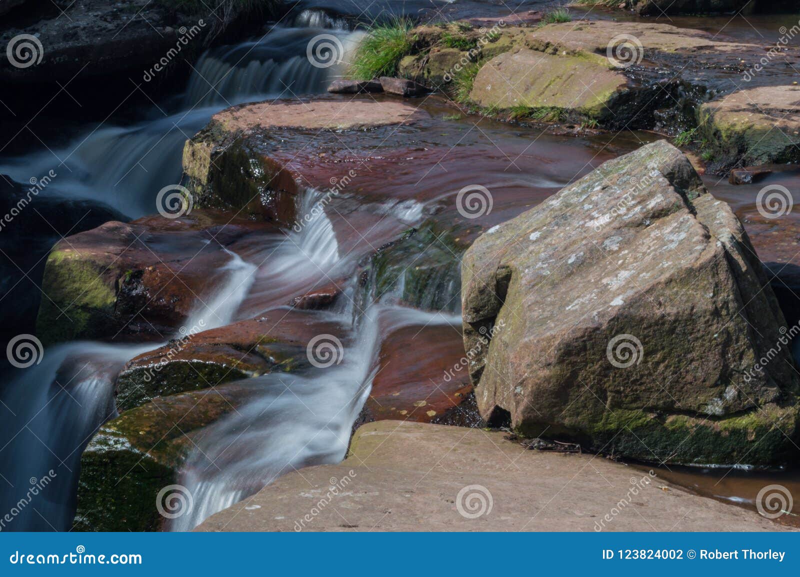 A Long Exposure of Small Waterfall Cascade Over Green and Brown Rocks ...