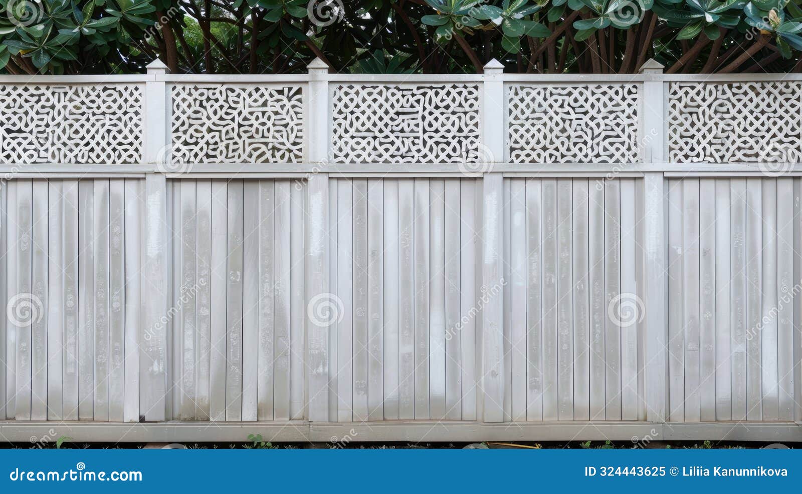 A Long White Lattice Fence Lines a Paved Path with Green Trees on ...