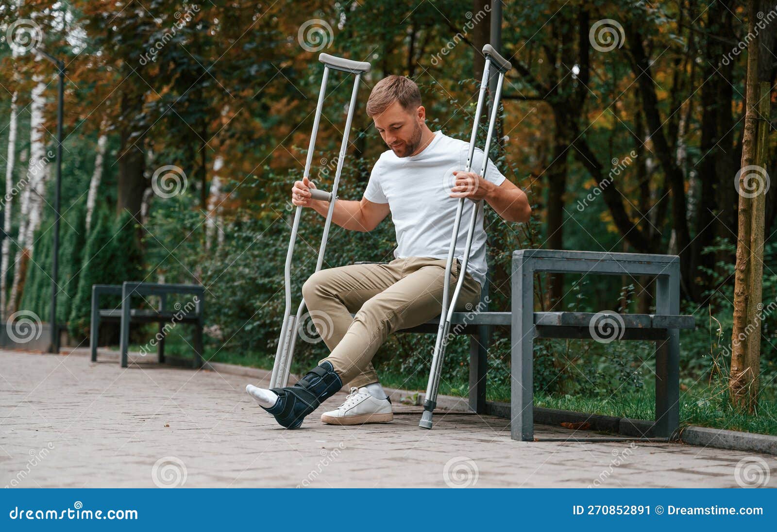 Looking at the Broken Leg. Man with Crutches is in the Park Outdoors ...