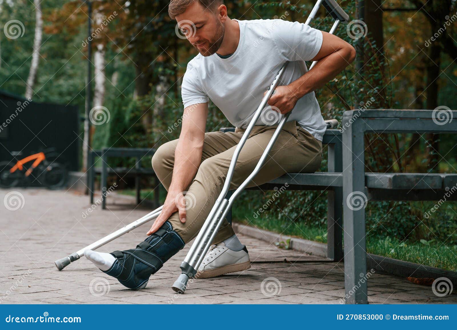 Looking at the Broken Leg. Man with Crutches is in the Park Outdoors ...