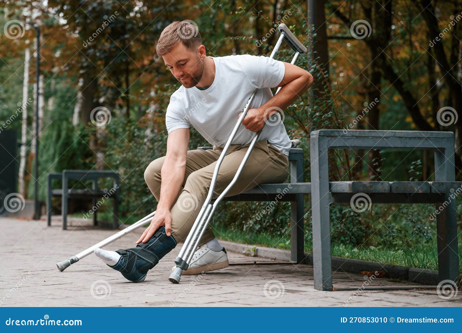 Looking at the Broken Leg. Man with Crutches is in the Park Outdoors ...
