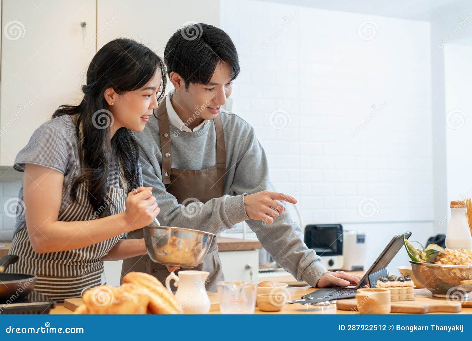 A Lovely Asian Couple Is Reading A Pastry Recipe On A Tablet Enjoying
